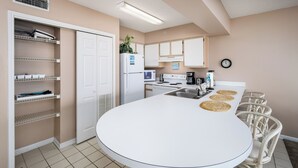 Cozinha com ilha central, armários brancos, micro-ondas e geladeira.