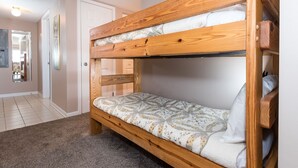 Uma cama beliche com edredom e almofadas estampadas, cabeceira de madeira e piso coberto por carpete.