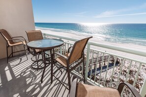 Varanda com mesa redonda e quatro cadeiras de vime, com vista para uma praia e o oceano.