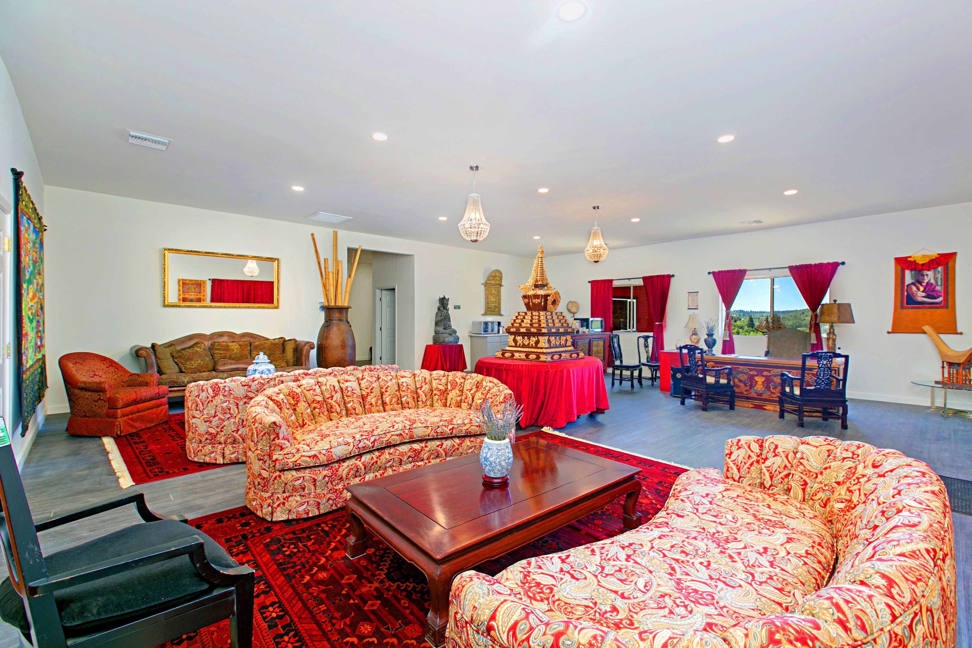 Uma sala de estar ampla com um conjunto de sofá estampado em vermelho e dourado, uma mesa de centro de madeira e uma área de jantar com cortinas vermelhas e uma mesa.
