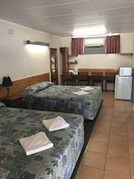 Quarto com duas camas, um pequeno espaço de cozinha, uma escrivaninha de madeira e um espelho.