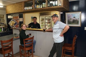 Uma área de bar com cadeiras de madeira, um balcão e prateleiras com garrafas.