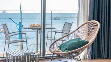 Uma varanda com cadeiras de vime, uma mesa com frutas e vista para o mar.