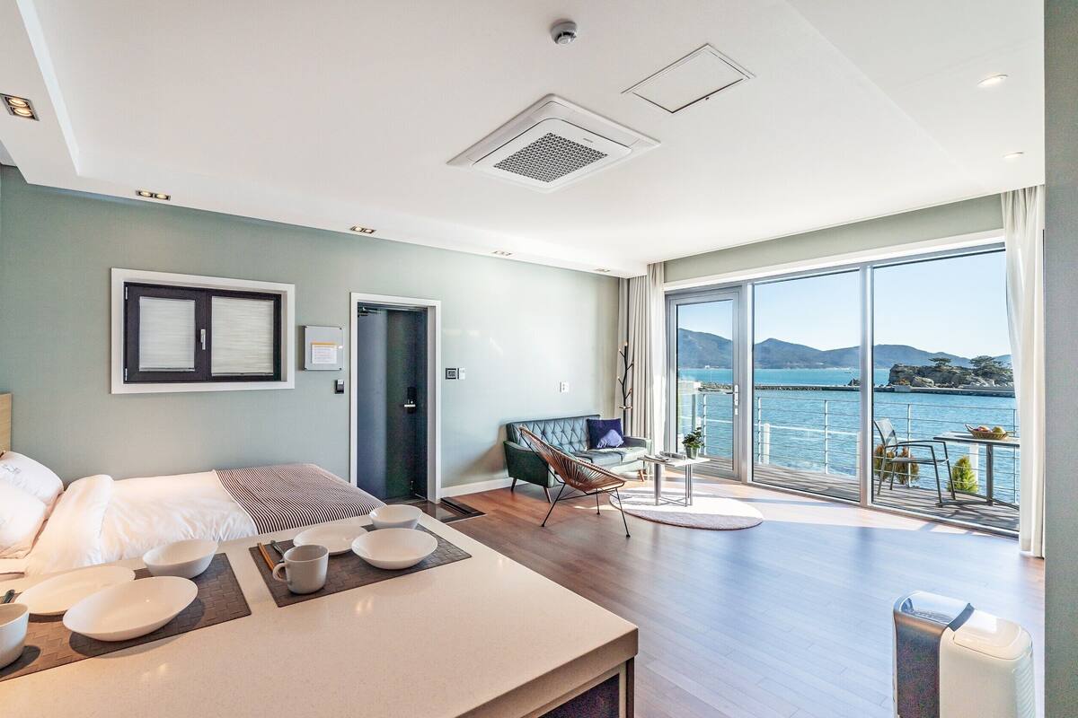 Quarto de hotel moderno com cama, área de refeições e varanda com vista para o mar.