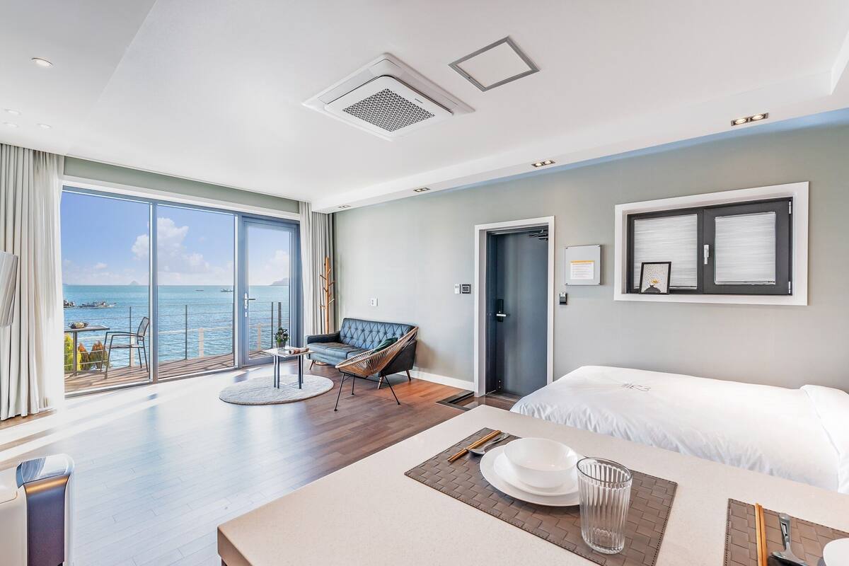 Quarto de hotel com varanda, cama, área de refeições e vista para o mar.