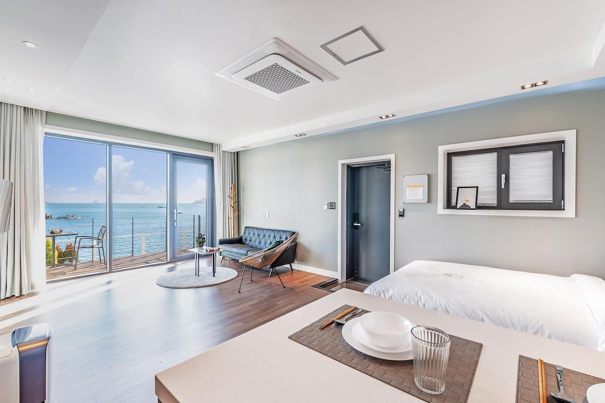 Quarto de hotel com varanda, cama, mesa de jantar e vista para o mar.