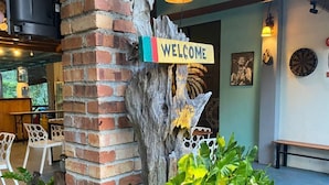 Um pilar de tijolos com uma placa de 'WELCOME', uma decoração de parede em madeira e uma planta verde em um quarto com um alvo de dardos e um banco.