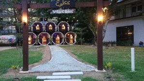 Entrada de um edifício com um letreiro de 'Bem-vindo', um caminho que leva à entrada e uma série de janelas iluminadas.