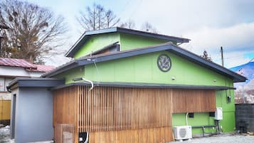 Um edifício com fachada verde, cerca de madeira e aparelho de ar condicionado.