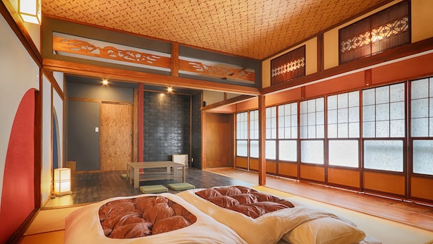 Um quarto japonês tradicional com tatame, futon, portas deslizantes e vista para o exterior por grandes janelas.