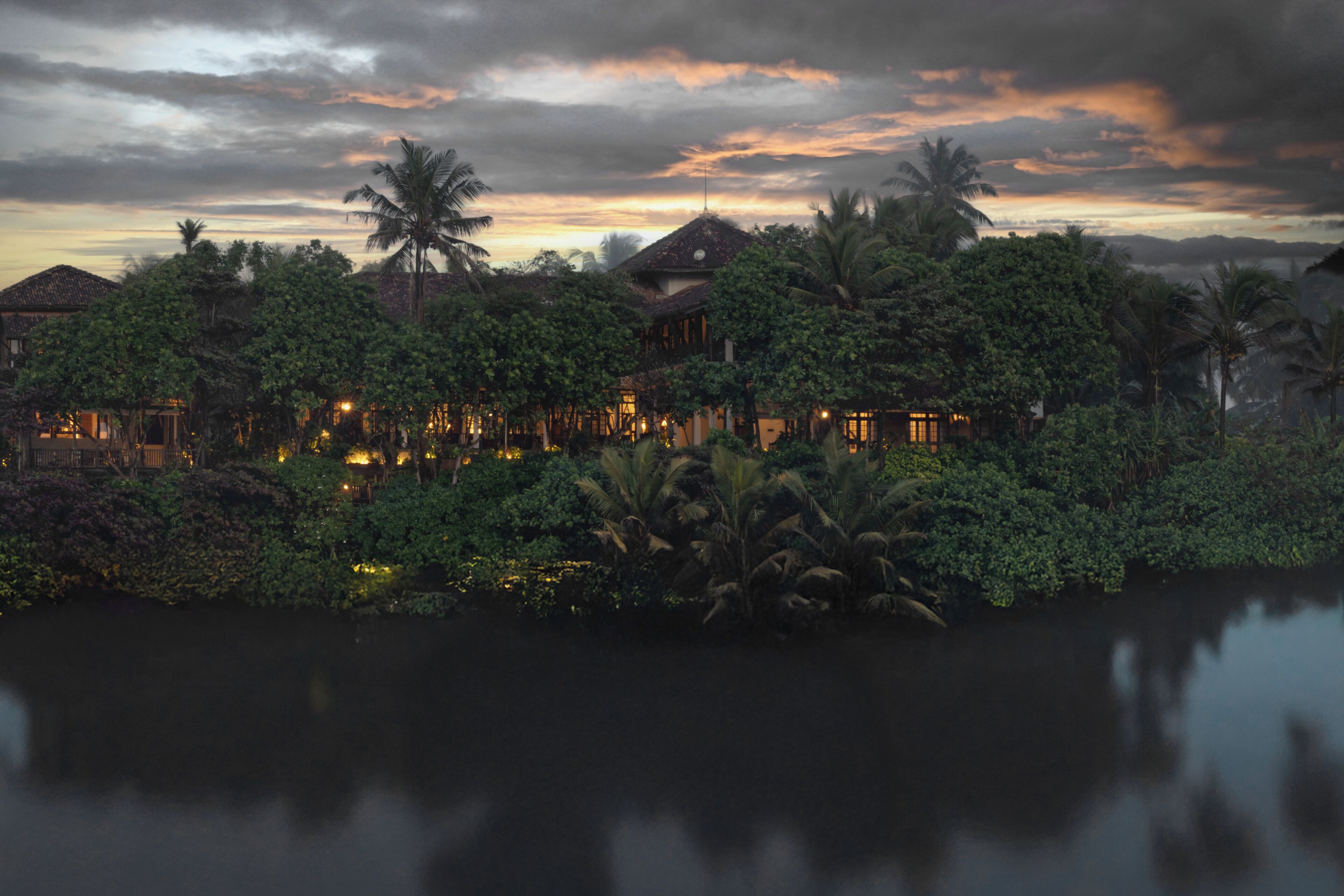 Um resort com vários edifícios rodeado por vegetação tropical exuberante e uma área de água calma.