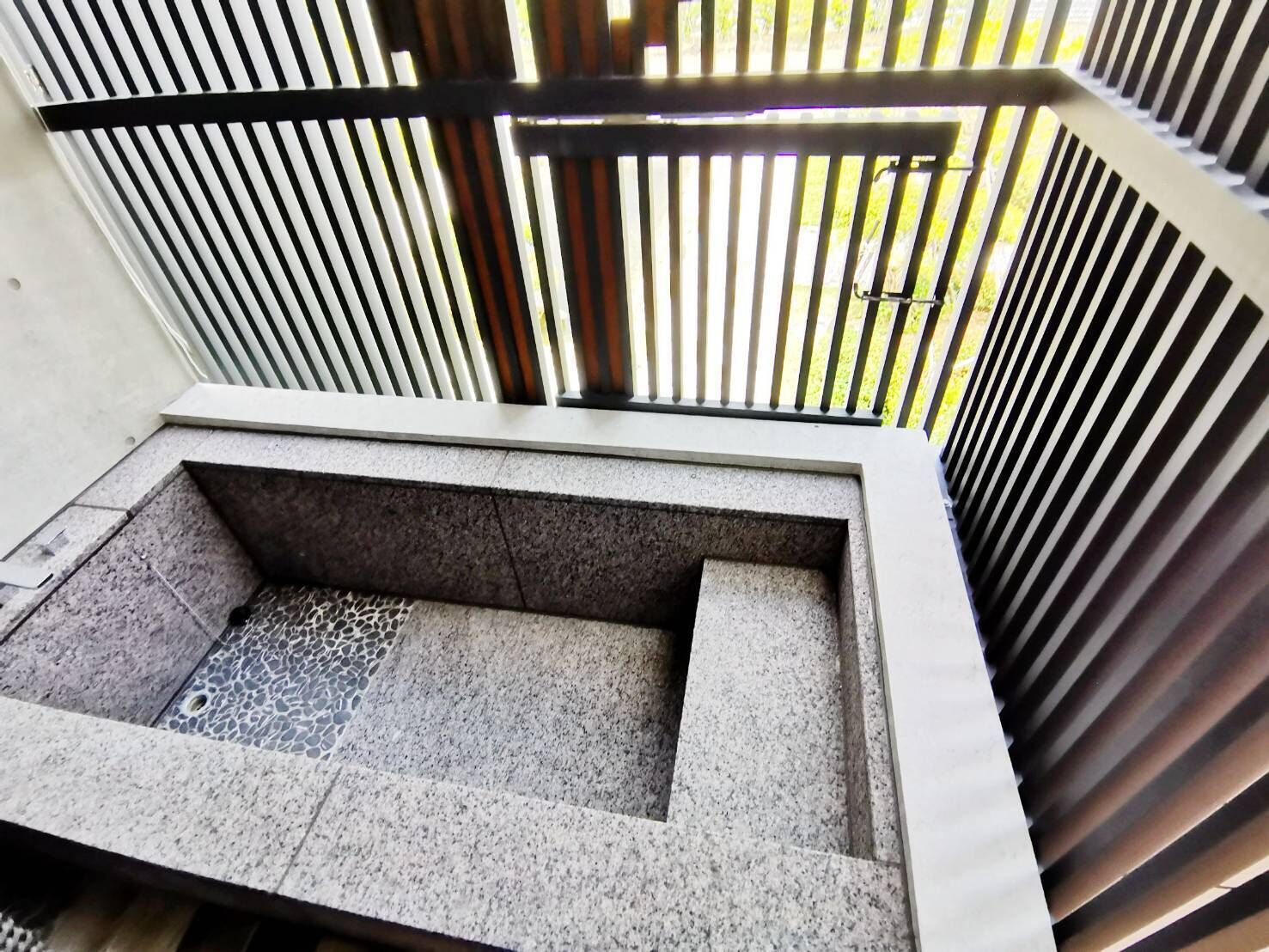 Um espaço ao ar livre pequeno e cercado, com chão de pedra e grade de metal.