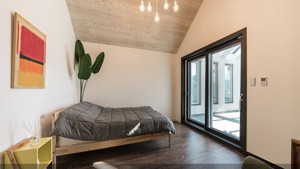 Um quarto moderno com cama, uma janela grande e uma planta.