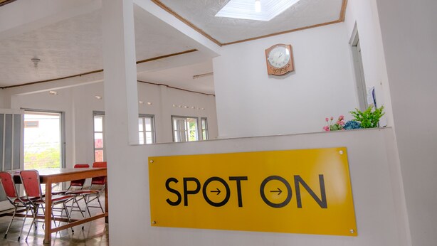 Uma sala de conferências com um letreiro amarelo 'SPOT ON', um relógio e vista para o exterior através de grandes janelas.