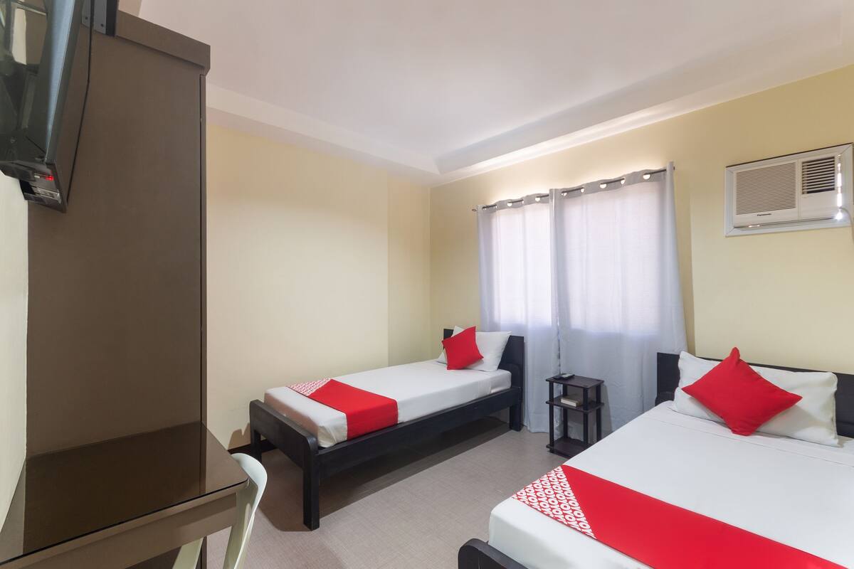 Quarto de hotel com duas camas de solteiro, uma escrivaninha, uma cadeira, uma televisão e ar condicionado.