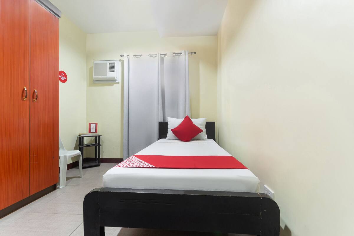 Quarto de hotel com cama, guarda-roupa, pequena mesa e unidade de ar condicionado.