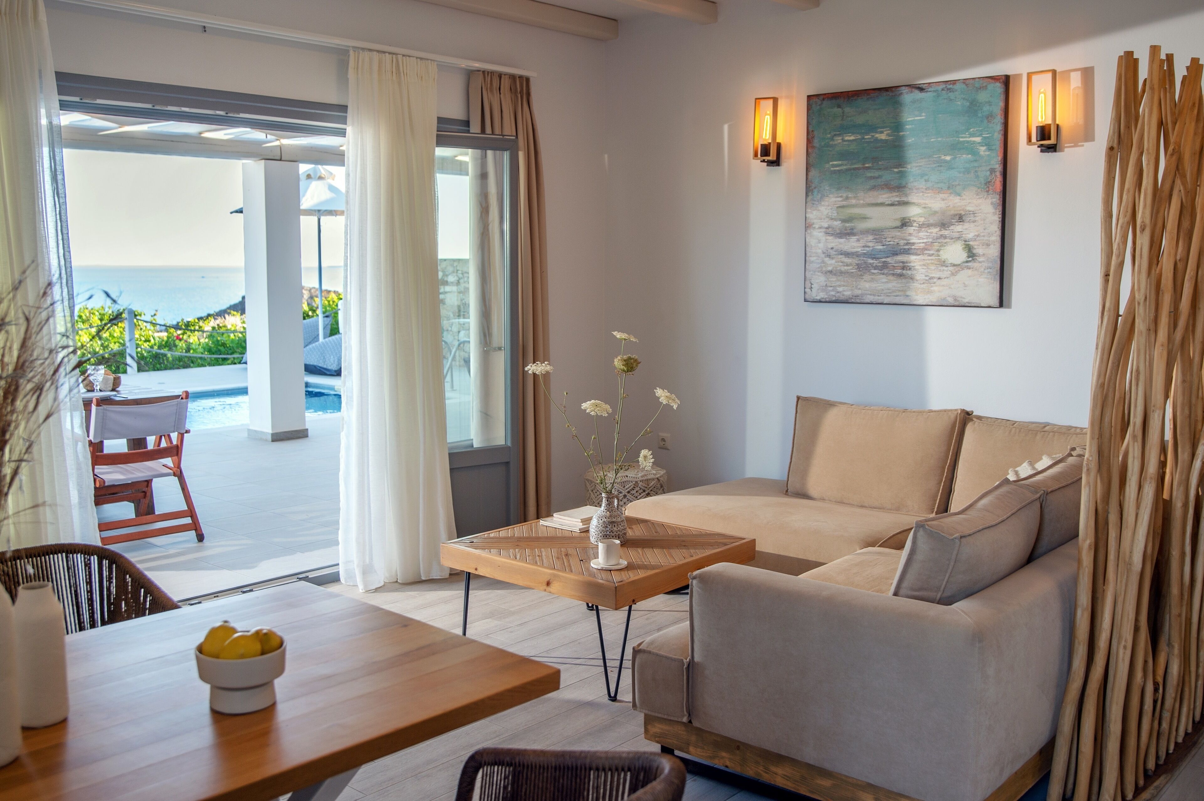 Uma sala de estar moderna com um sofá, uma mesa de centro de madeira e vista para o oceano através de amplas janelas.
