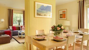 Uma sala de jantar com uma mesa de madeira posta para quatro pessoas, um vaso de flores e um quadro acima da mesa.