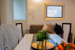 Uma sala de estar moderna com um sofá, uma mesa de centro com uma planta e tomates, e um quadro na parede.