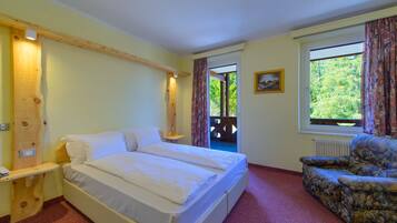 Quarto com cama de casal, mesa de cabeceira de madeira, uma cadeira e uma janela com cortinas.
