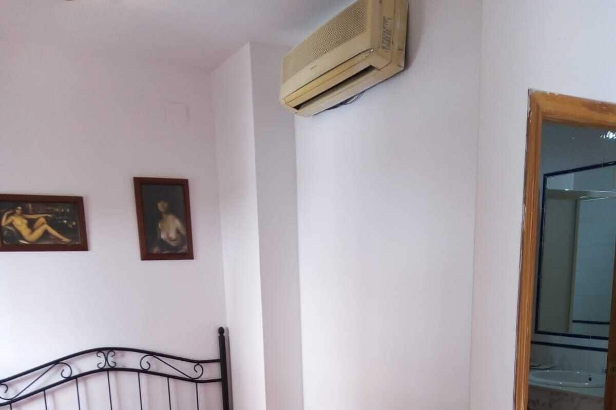 Quarto com uma cama de solteiro, uma porta de madeira e um aparelho de ar condicionado na parede.
