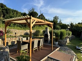 Uma pérgola de madeira com mobiliário de vime e uma chaminé de pedra.