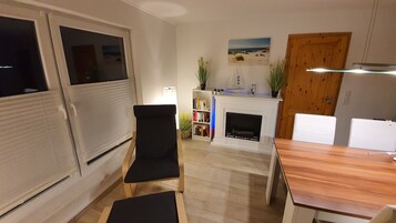 Uma sala de estar moderna com lareira, estante de livros e área de jantar com mesa e cadeiras de madeira.
