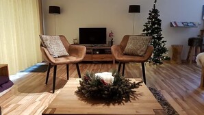Uma sala de estar com duas poltronas de couro marrom, uma mesa de centro de madeira com decoração natalina, uma televisão e uma árvore de Natal.