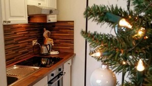 Uma cozinha com armários de madeira, uma pia de aço inoxidável e um pinheiro de Natal branco com luzes.
