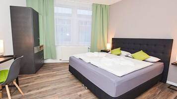 Quarto de hotel com uma cama, uma escrivaninha, uma cadeira e um guarda-roupa.