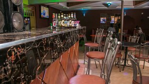 Uma área de bar com bancada de mármore, diversas garrafas de bebidas e cadeiras de metal.