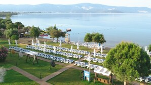 Resort à beira do lago com fileiras de espreguiçadeiras e guarda-sóis, uma torre de salva-vidas e vista para o lago e montanhas.