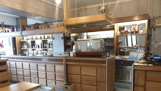 Um restaurante acolhedor com mobiliário de madeira, um espaço de bar com garrafas e uma máquina de café.