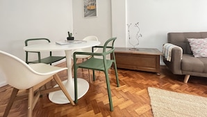 Sala de estar moderna com mesa de jantar redonda, cadeiras verdes, sofá cinza e mesa de centro de madeira.