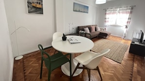 Uma sala de estar moderna com uma mesa de jantar redonda, cadeiras verdes e brancas, um sofá e uma grande janela com cortinas.