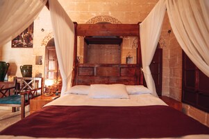 Quarto tradicional com cabeceira de madeira, cama com roupa de cama branca e cortinas drapeadas.