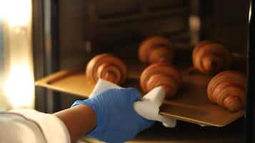 Pessoa usando uma luva azul manuseando uma bandeja com croissants dentro de um forno.