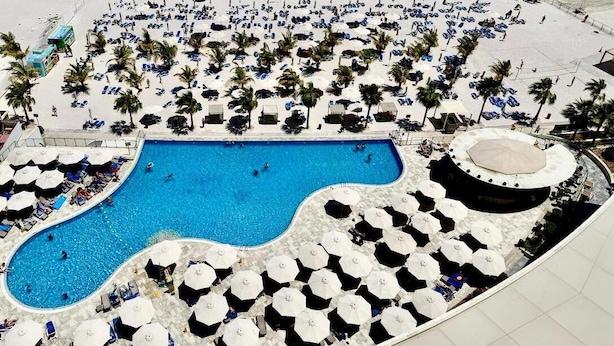 Resort com uma piscina grande, área de praia com espreguiçadeiras e um lago circular.