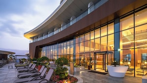 Um hotel moderno com fachada curva, área externa com cadeiras de lounge e entrada bem iluminada.