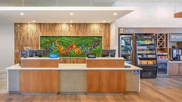 Balcão de recepção de hotel com acabamento em madeira, um visor digital e uma obra de arte floral fixada na parede.