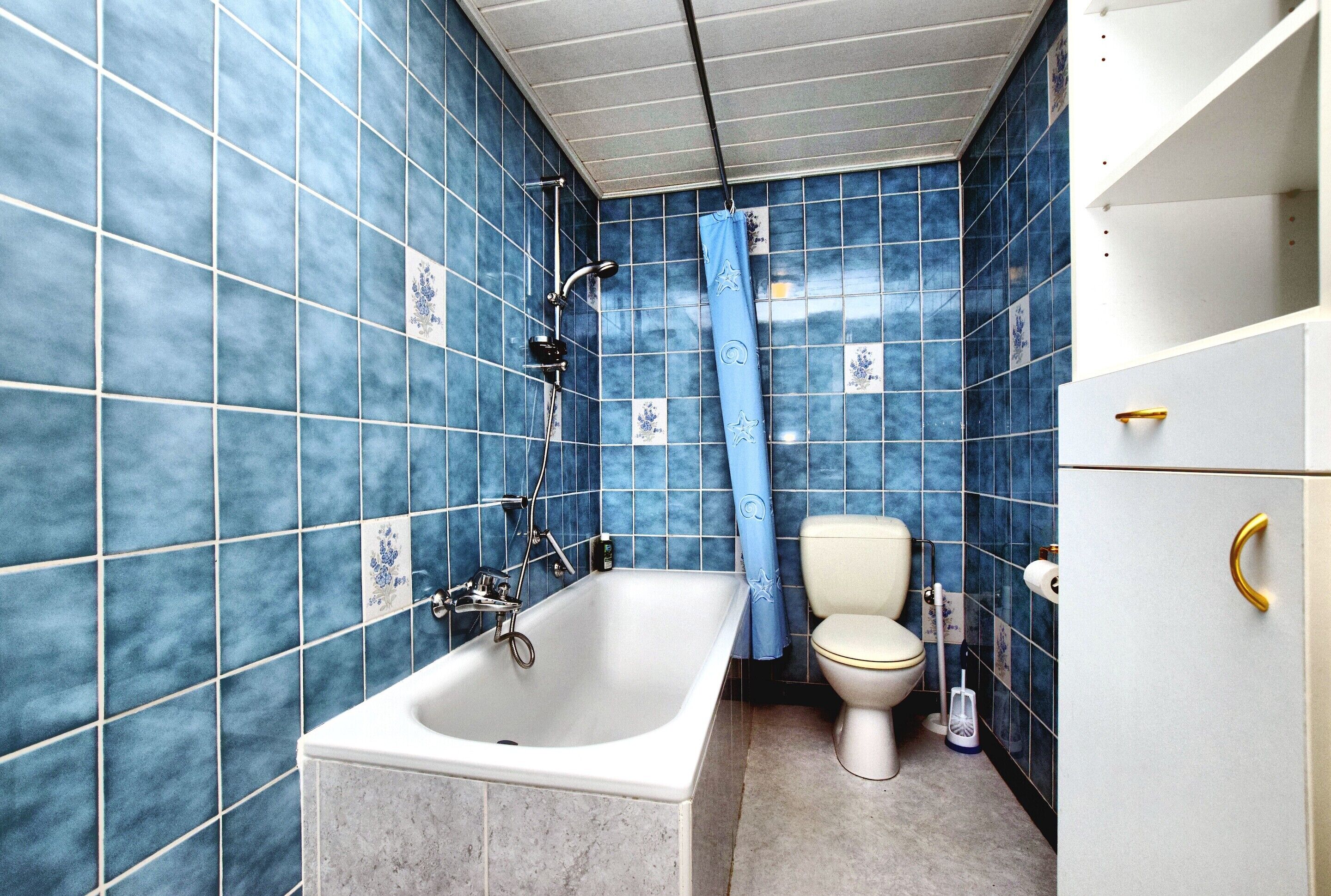 Uma casa de banho com azulejos azuis, uma banheira branca, uma sanita e um chuveiro.