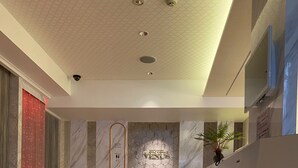 Um hall de hotel com piso de mármore, uma mesa de recepção, uma placa indicando quarto de hóspedes e uma parede com padrões hexagonais.