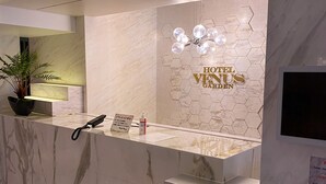 Balcão de recepção de hotel com design em mármore, um vaso de planta, uma placa e um candelabro.
