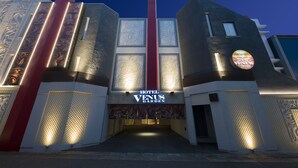 Exterior do Hotel Venus Garden com design moderno, destacando uma marcante faixa vertical vermelha e desenhos decorativos na fachada.