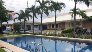 Piscina com duas escadas de metal, rodeada por palmeiras e um edifício com telhado de azulejos.