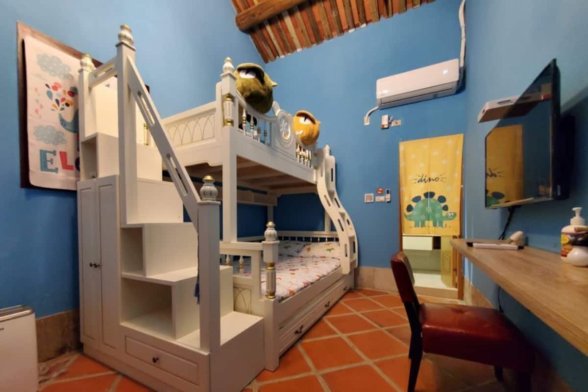 Uma cama beliche com escrivaninha e cadeira, um espelho e uma decoração de parede com tema de dinossauro.