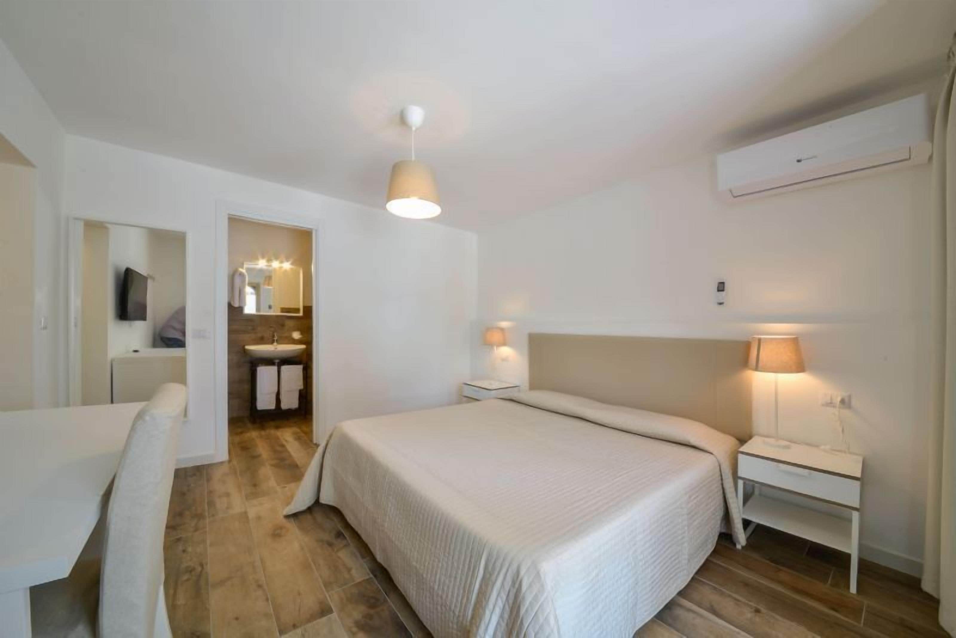 Quarto com cama, mesas de cabeceira, um espelho e um banheiro visível por uma porta aberta.