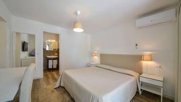 Quarto com cama, mesas de cabeceira, um espelho e um banheiro visível por uma porta aberta.