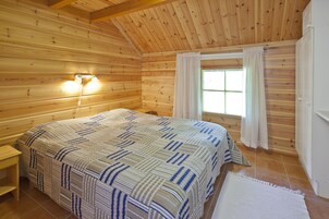 Quarto de cabana de madeira com cama, mesa de cabeceira, janela com cortinas e teto de madeira.