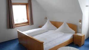 Uma cama de solteiro com roupa de cama branca num quarto com teto inclinado e janela com cortinas.
